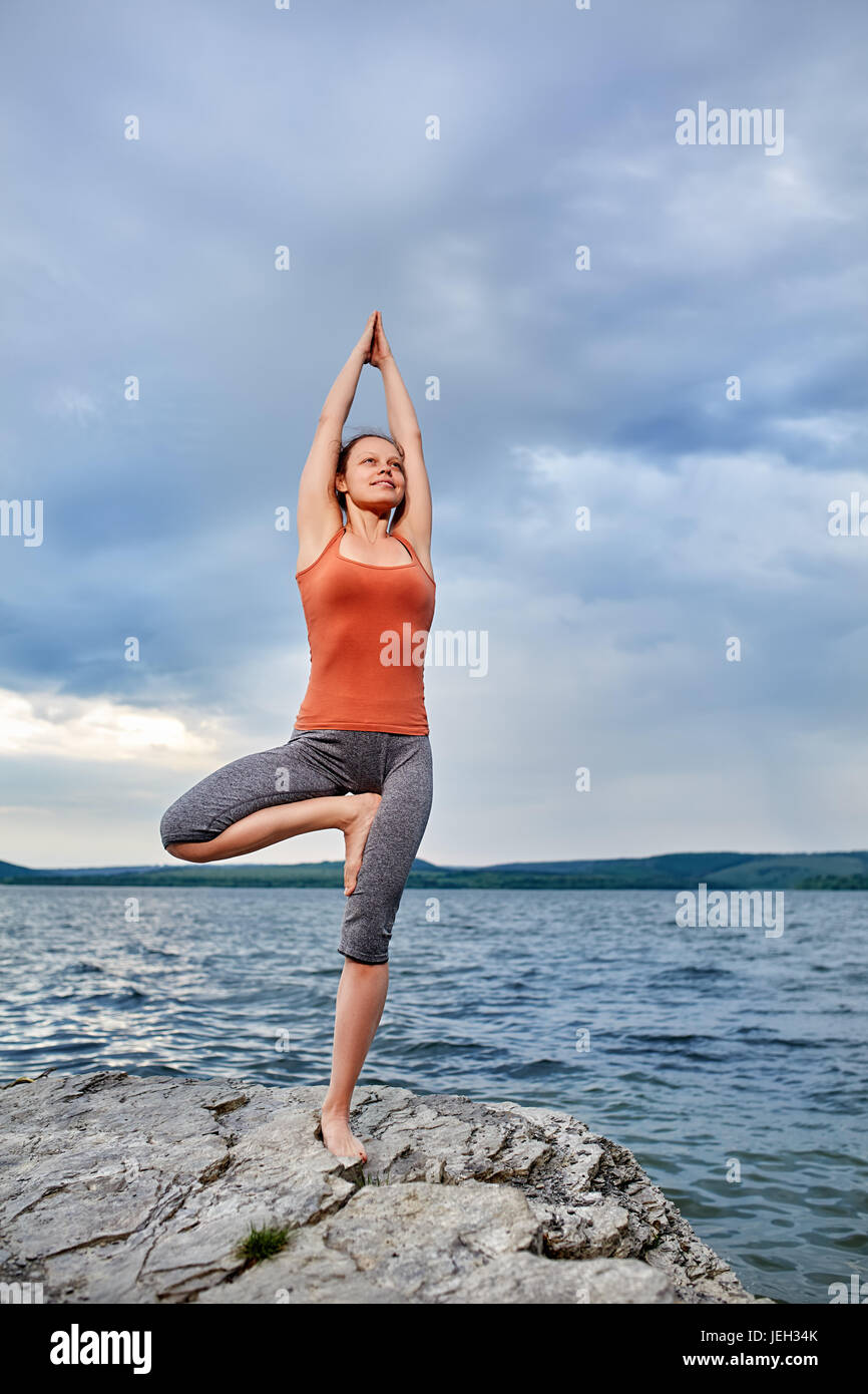 Young sporty woman doing different variants of yoga position on a rocky ...