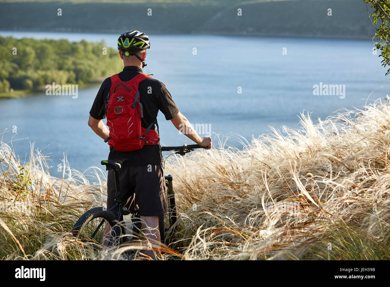 Rear view of the young cyclist standing with mountain bike against ...