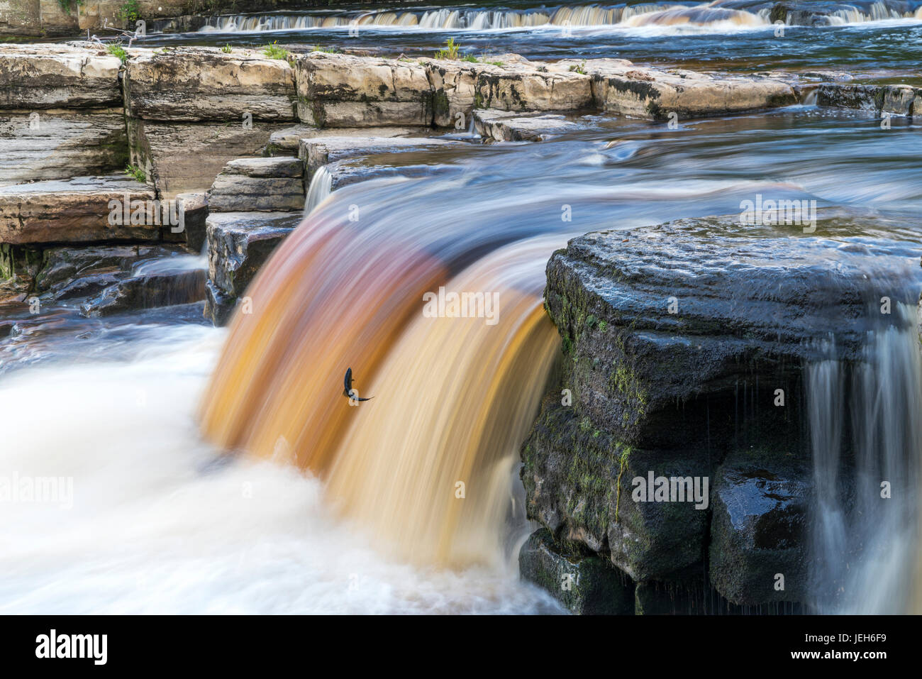 Coloured waterfall flowing over a cliff; Richmond, North Yorkshire ...
