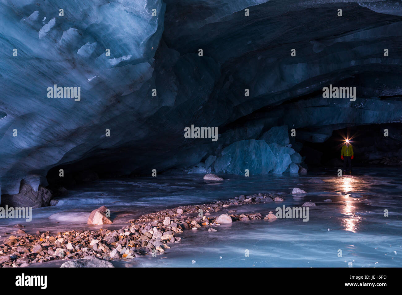 A man's headlamp reflects off the icy floor of a cavernous ice cave at ...