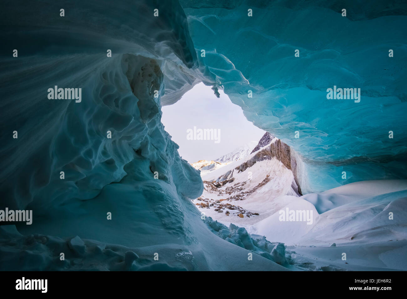 A wave-like formation of snow curls around the entrance of a small ice ...
