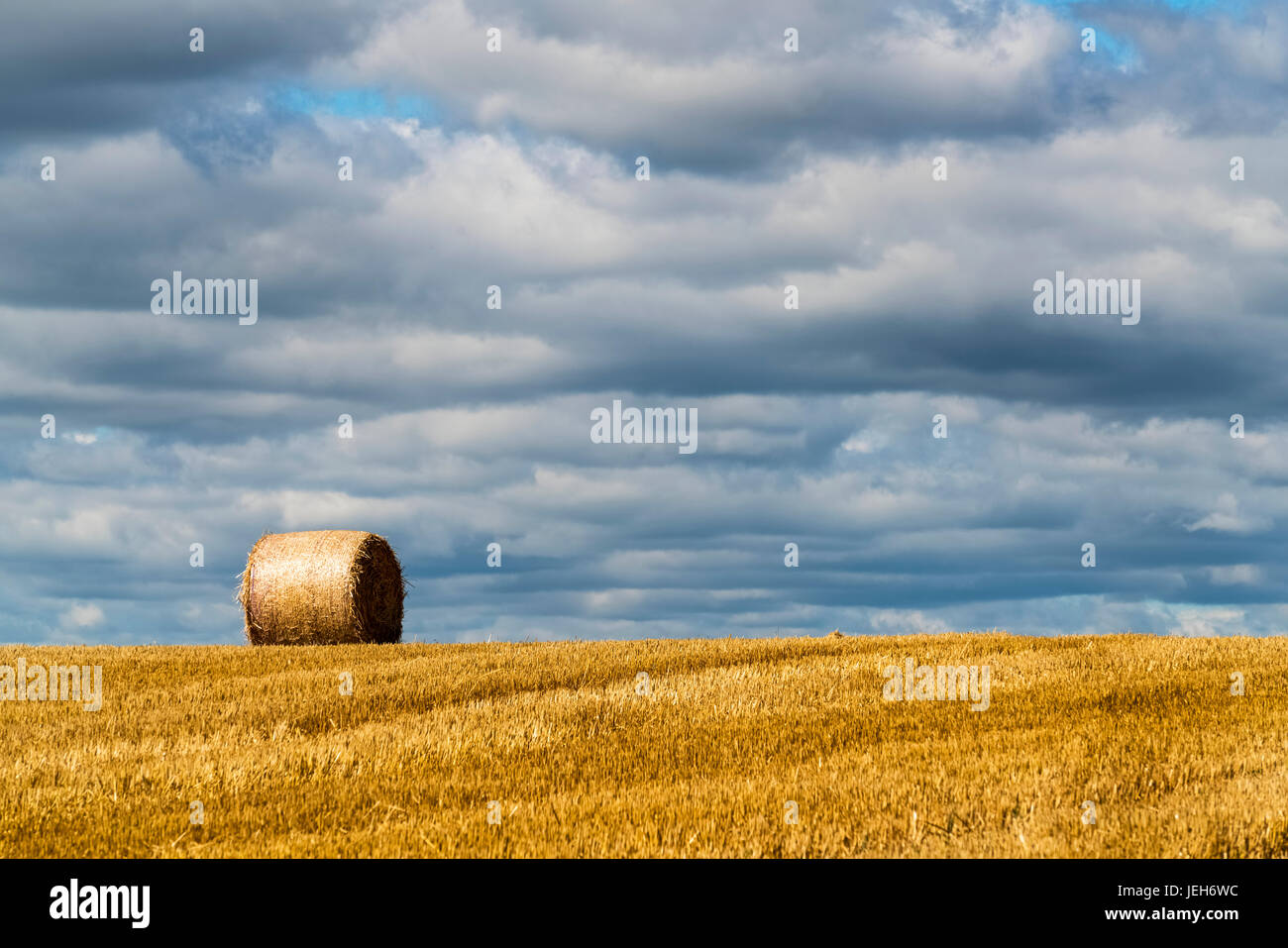 A single hay bale on a cut field under a cloudy sky; Ravensworth, North ...