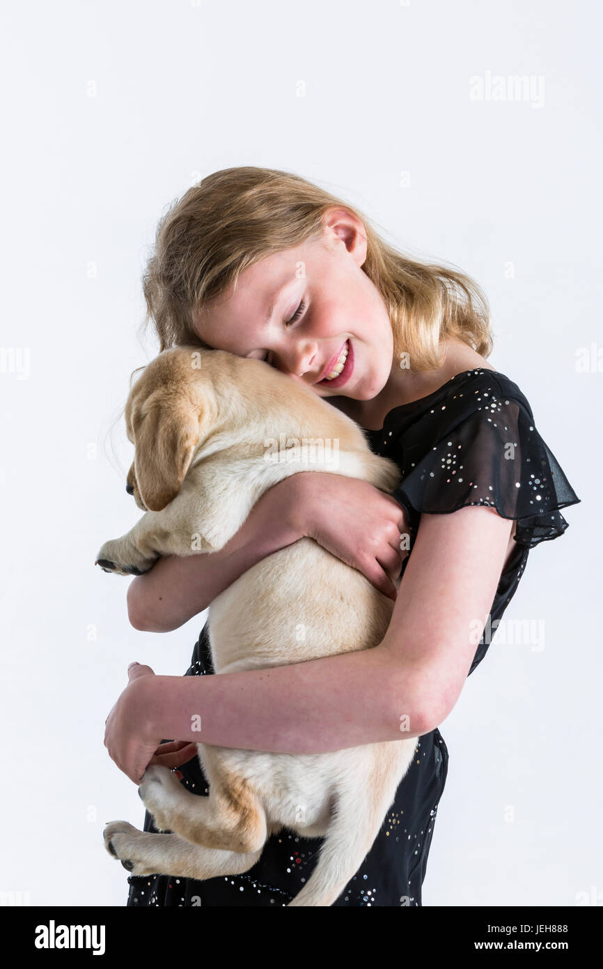 A smiling young girl hugs a Labrador puppy against a white background ...