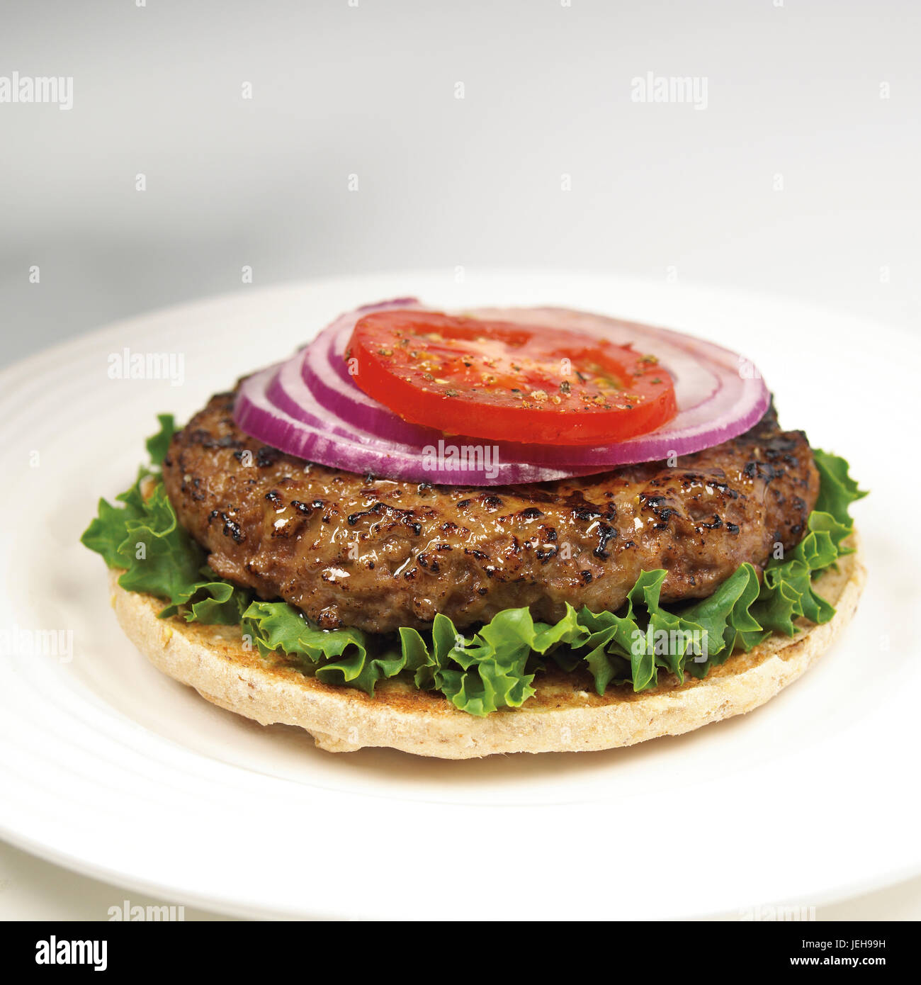 Hamburger patty with onion, lettuce and tomato on flatbread Stock Photo ...