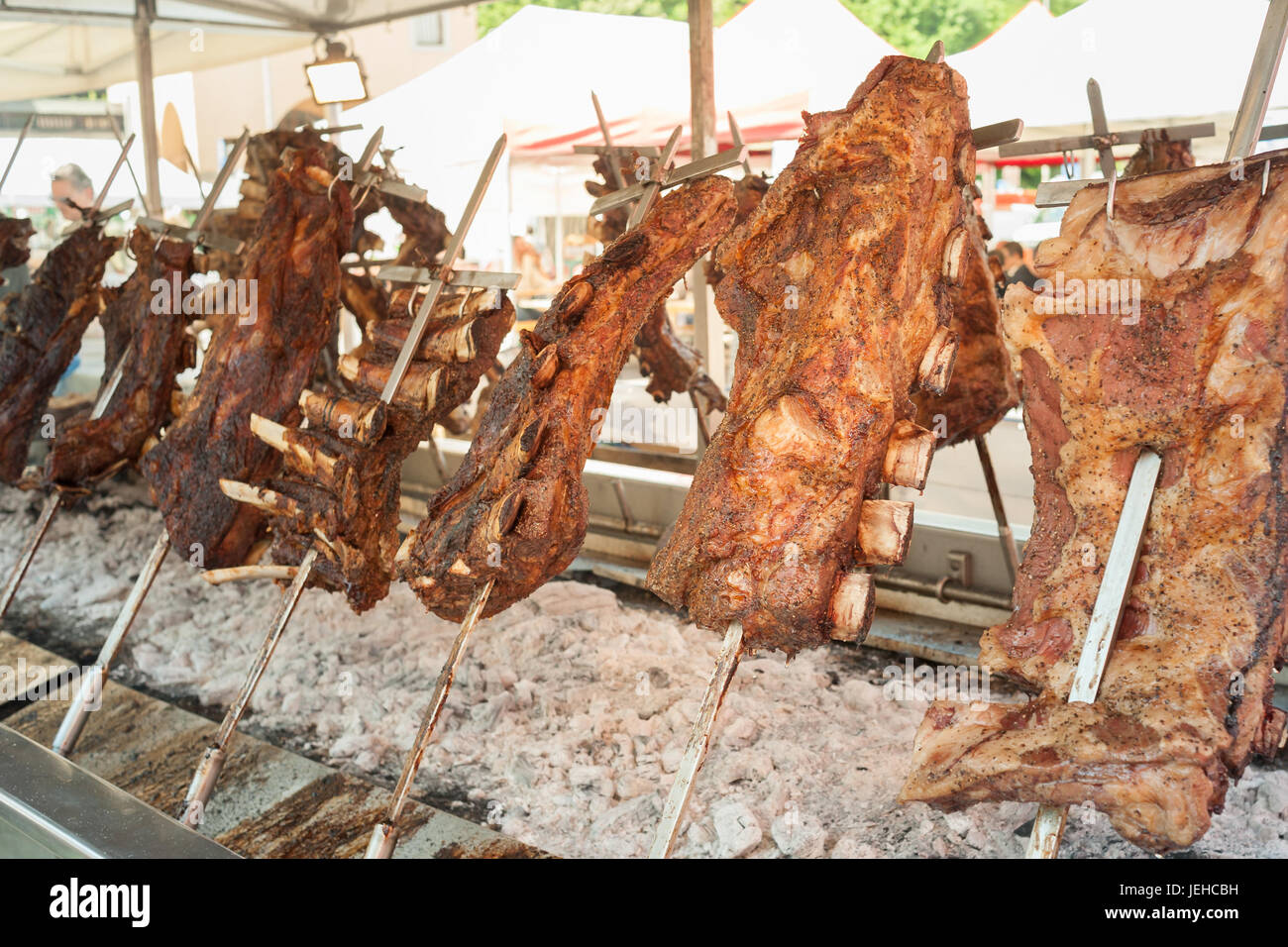 Roasted meat of beef cooked on a vertical grills placed around fire ...
