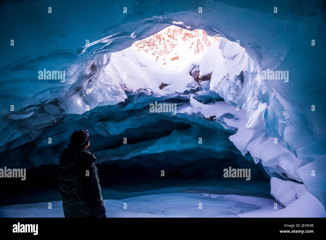 A man looks out an opening in the ceiling of an ice cave within ...