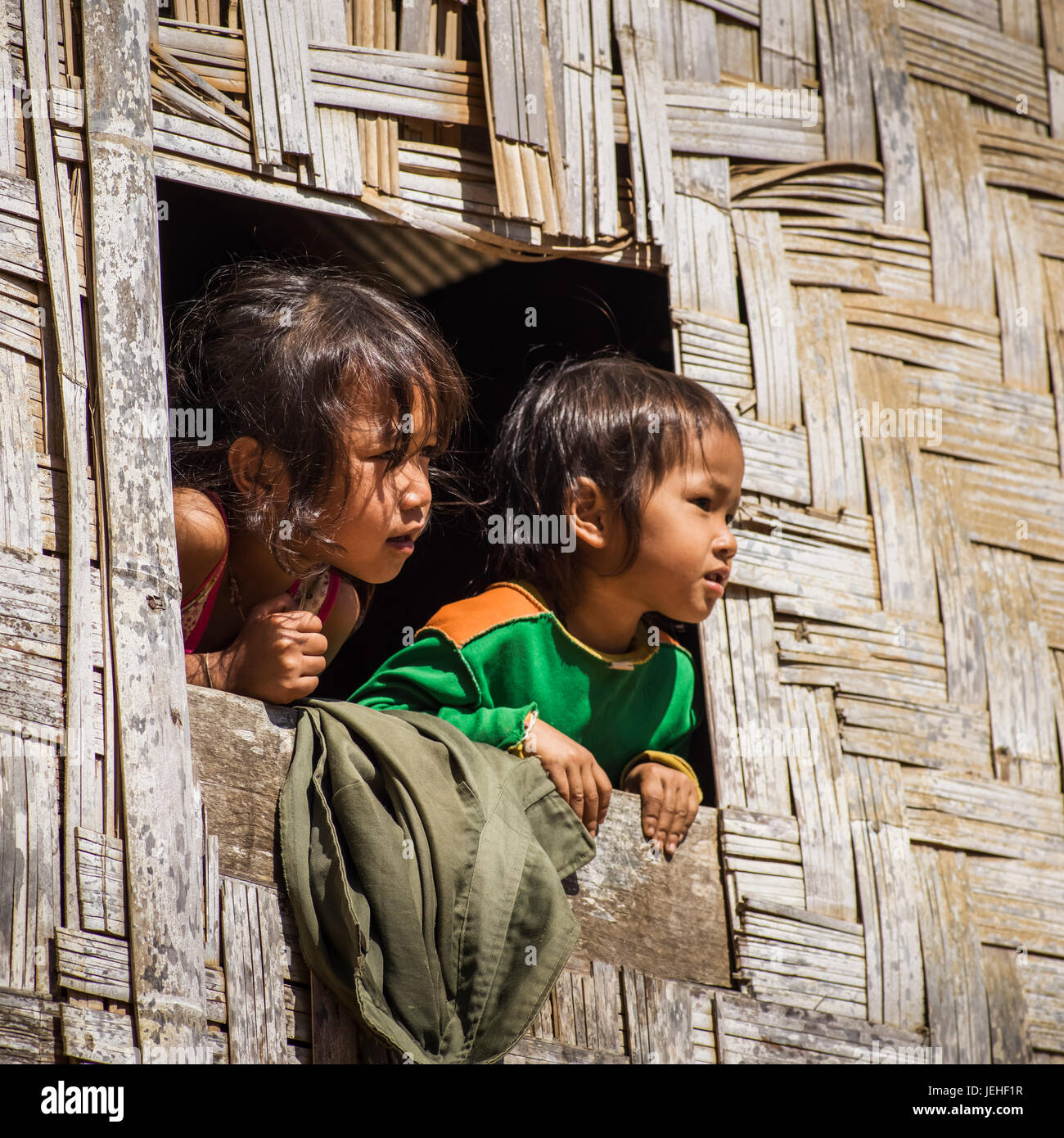 A young boy and girl lean out a window of a building with a woven ...