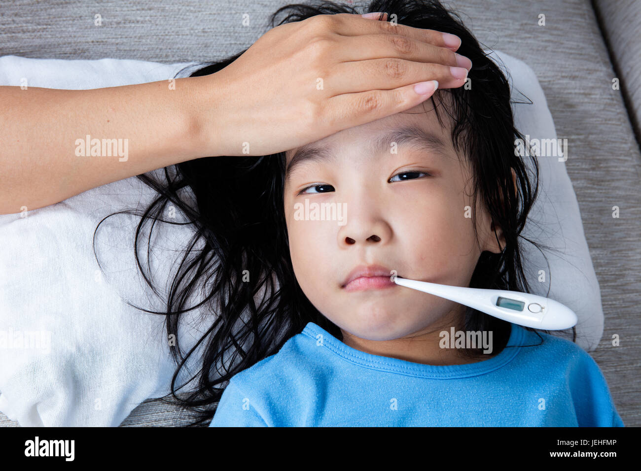Asian Chinese mother measuring little girl forehead for fever at home ...
