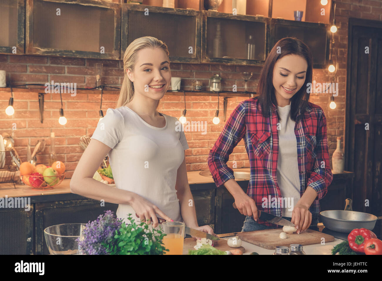 Young female friends cooking meal together at home cutting ingrediants ...