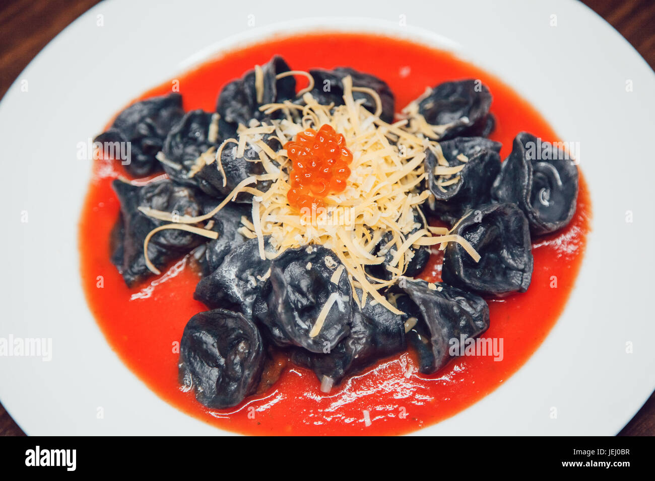 Black ravioli with salmon in tomato sauce decorated with cheese and red ...