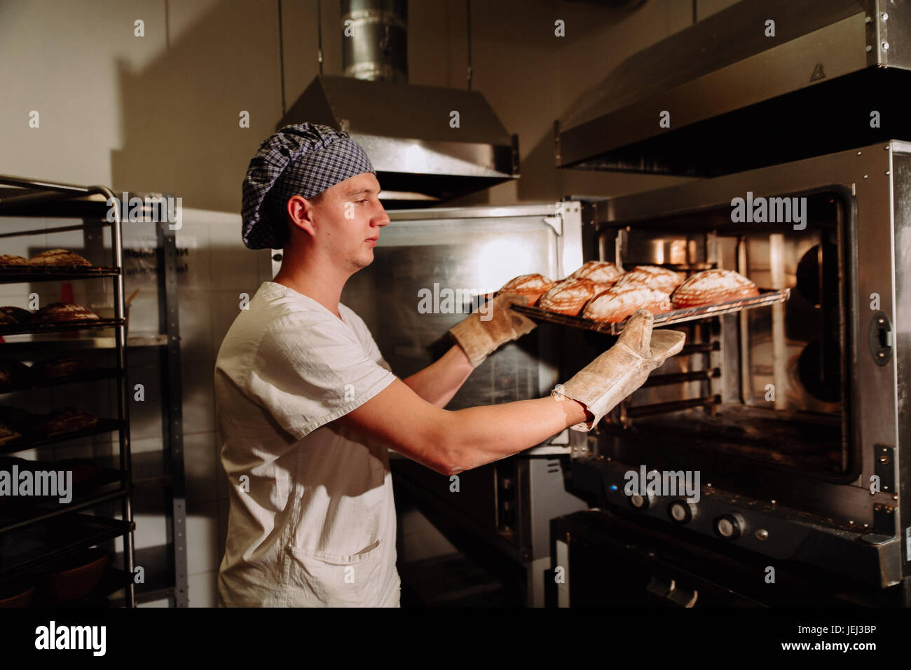 Handsome baker in uniform holding tray full of freshly baked bread at ...