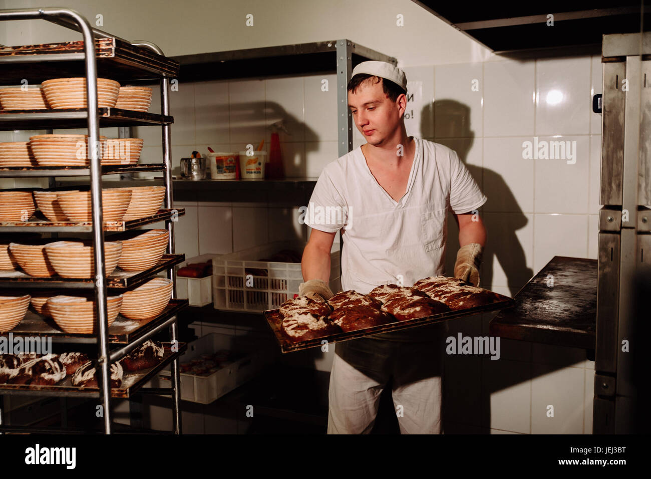 Handsome baker in uniform holding tray full of freshly baked bread at ...