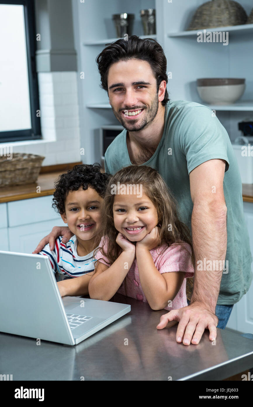 Smiling father using laptop with his children in kitchen Stock Photo ...