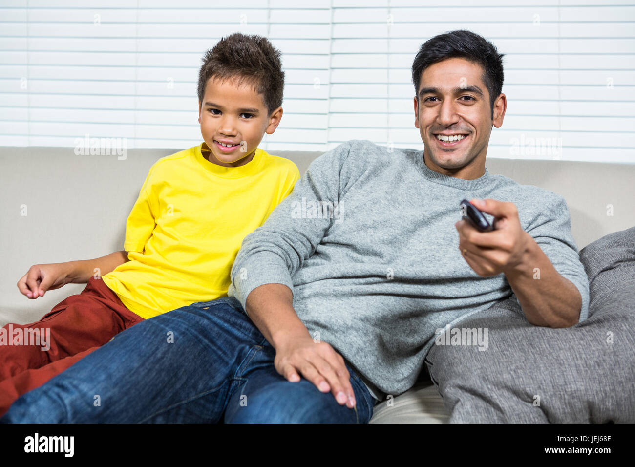 Smiling father ans son watching tv on the sofa Stock Photo - Alamy