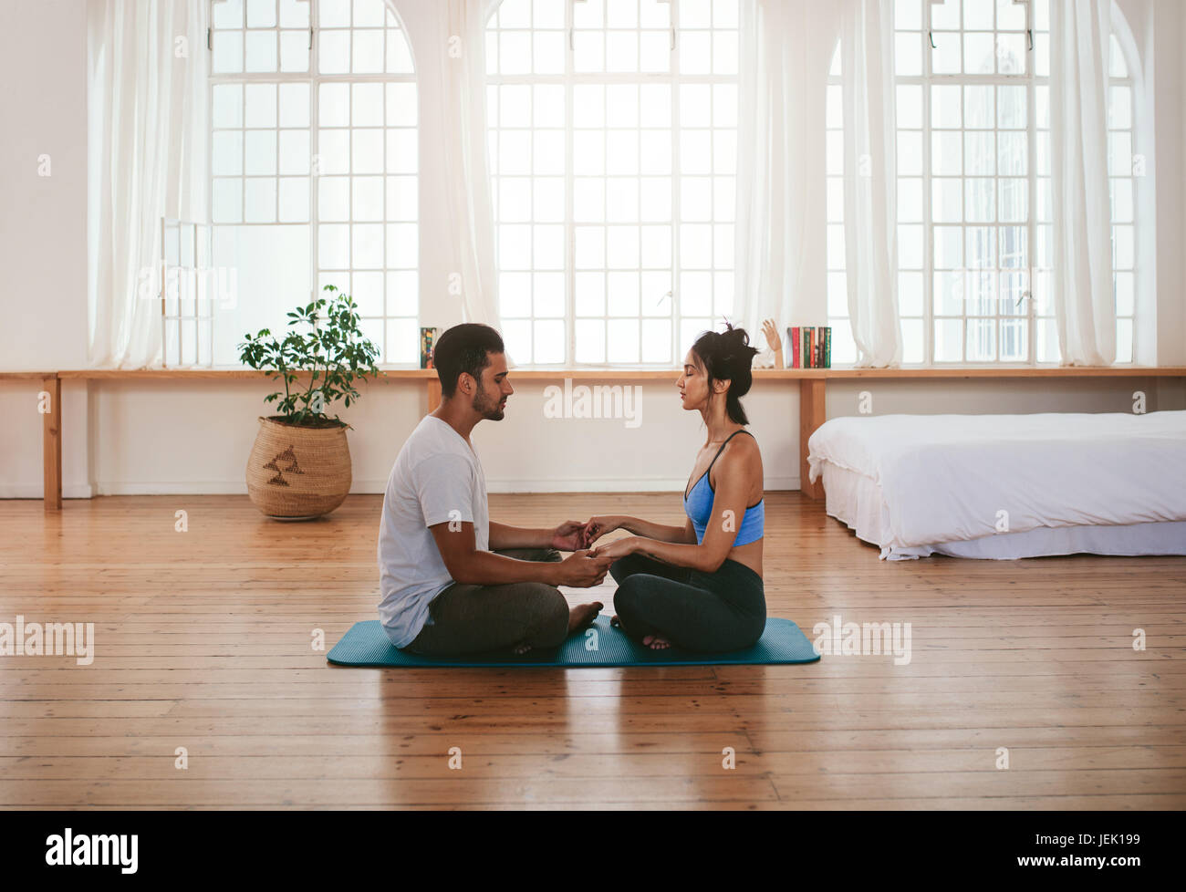 Side view of beautiful young couple doing yoga at home. They are ...