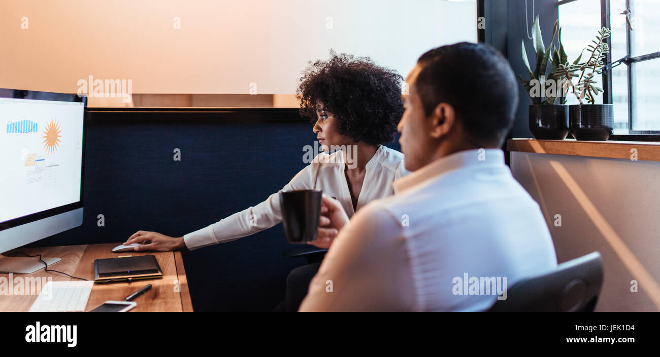 Two businesspeople looking together at computer. Young man and woman ...