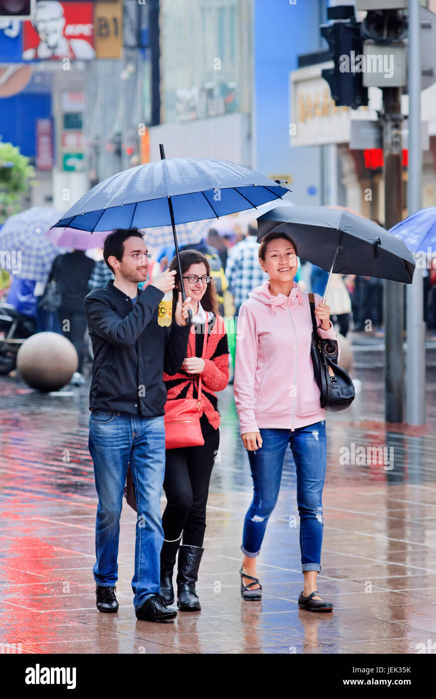 Caucasian couple and Chinese girl with umbrella in city center ...