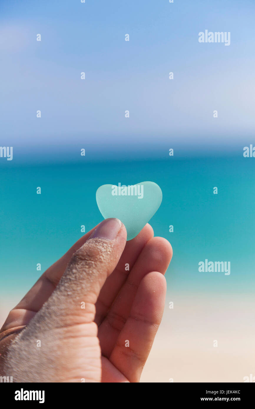 A Hand Holding A Turquoise Heart Shaped Sea Glass Against The Background Of The Turquoise Ocean 