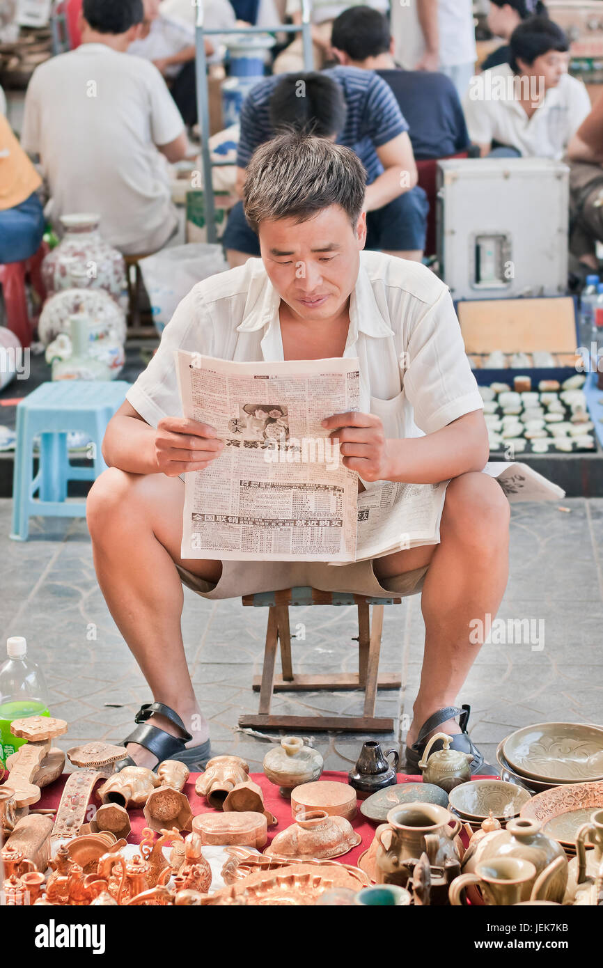 BEIJING–SEP. 8 2007. Chinese vendor reads newspaper on Panjiayuan ...