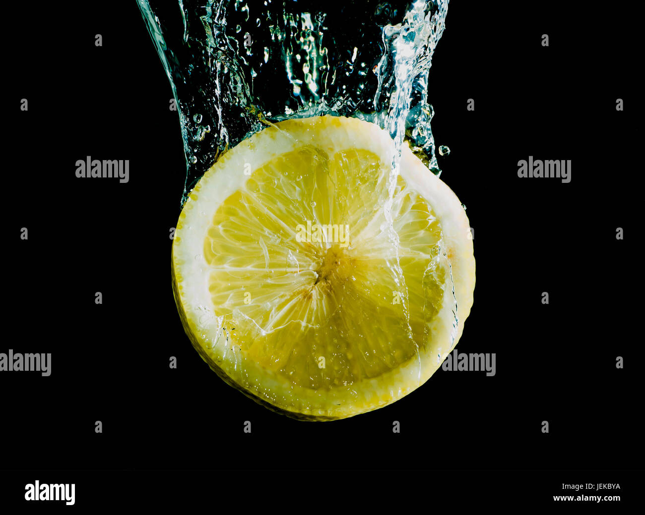 A slice of yellow lemon falls into the water on black background Stock ...