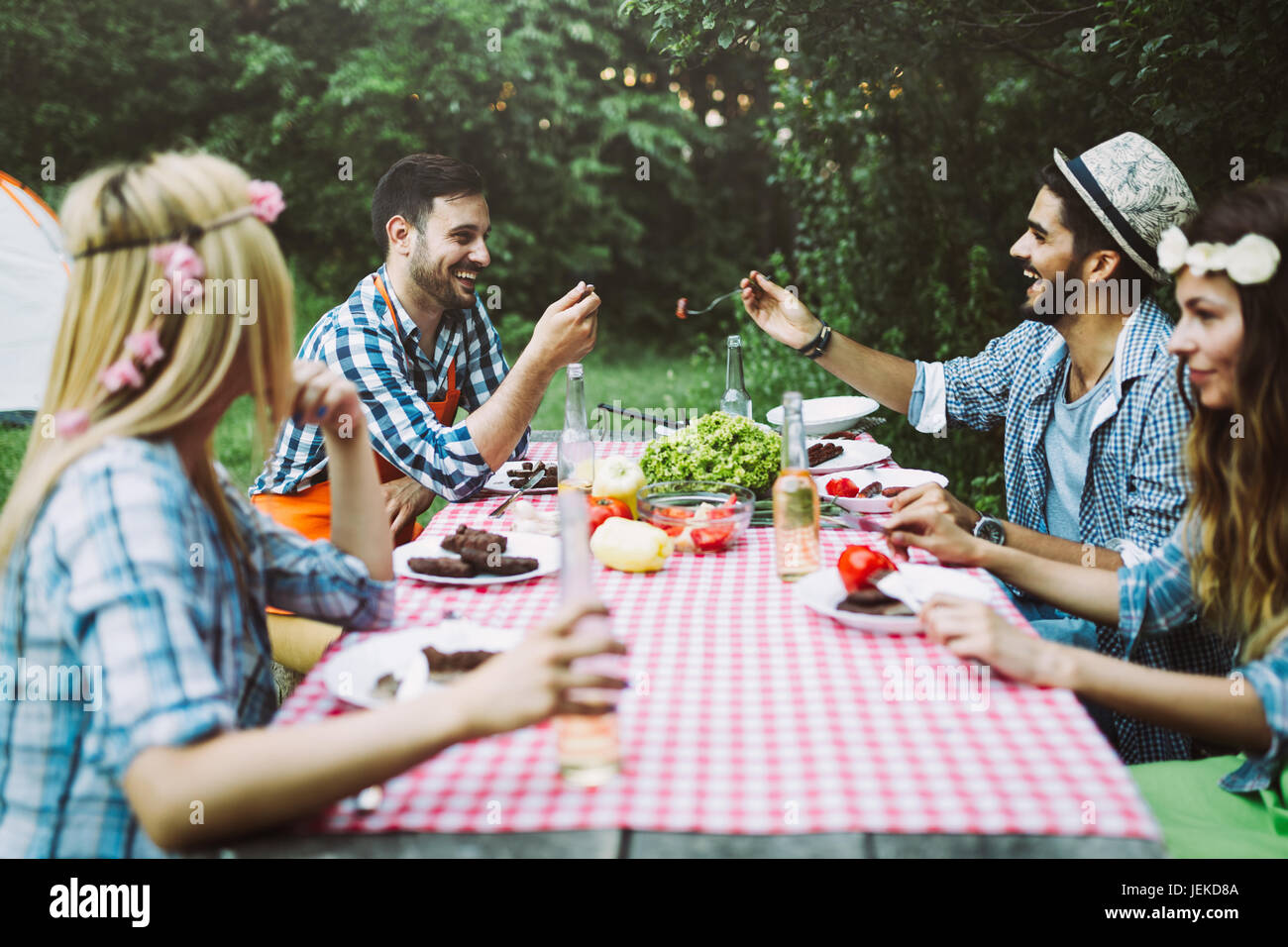 Cheerful friends sitting at table and having meal in nature Stock Photo ...