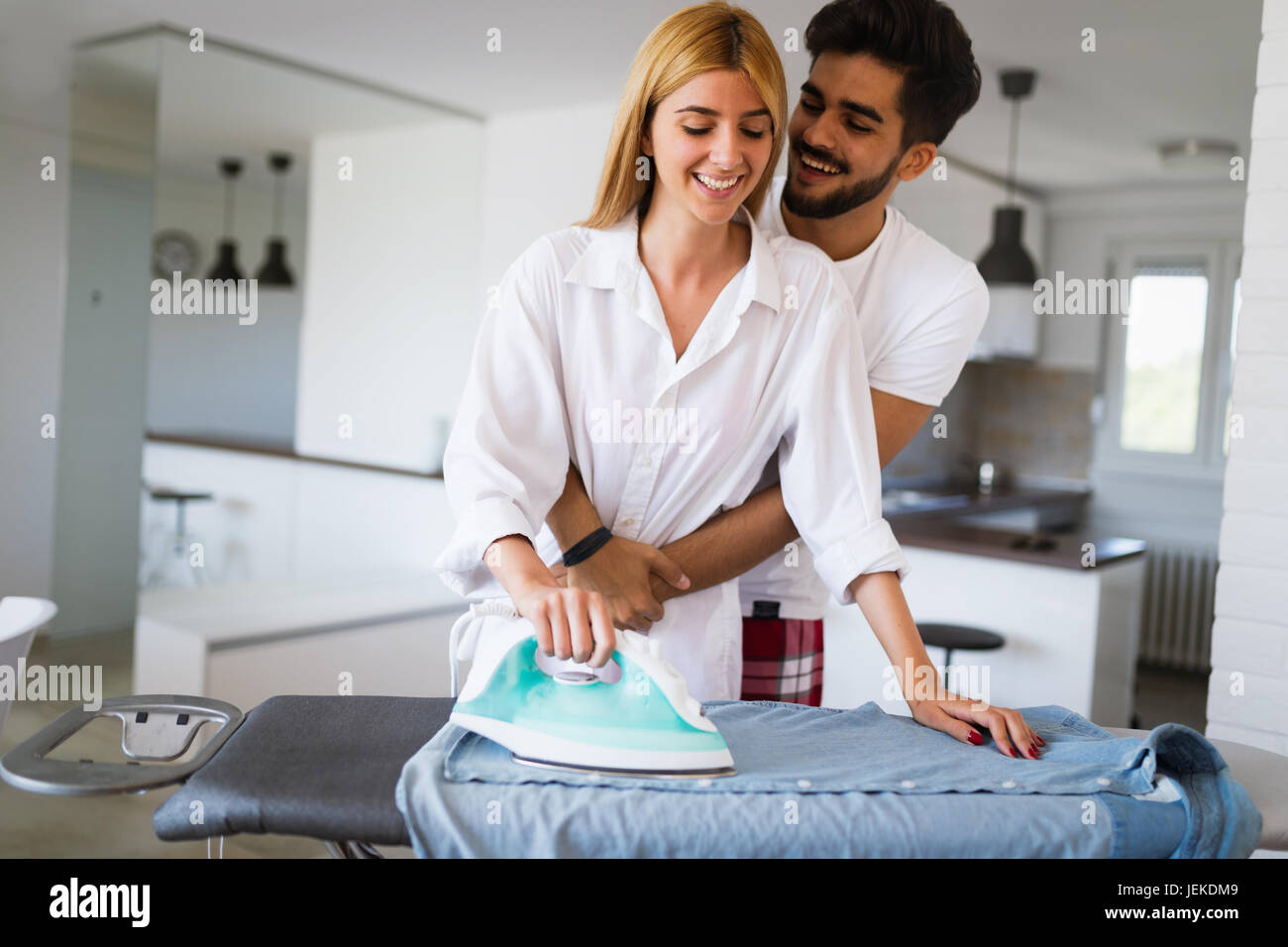 Young Attractive Man Hugging His Girlfriend While She Uses Iron Stock