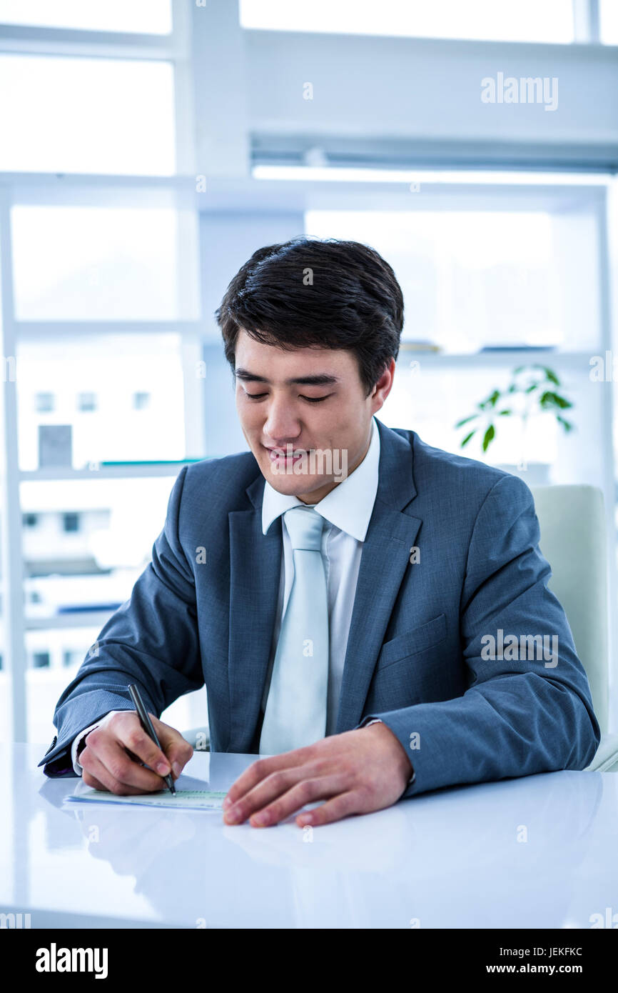 Smiling asian businessman completing a cheque Stock Photo - Alamy