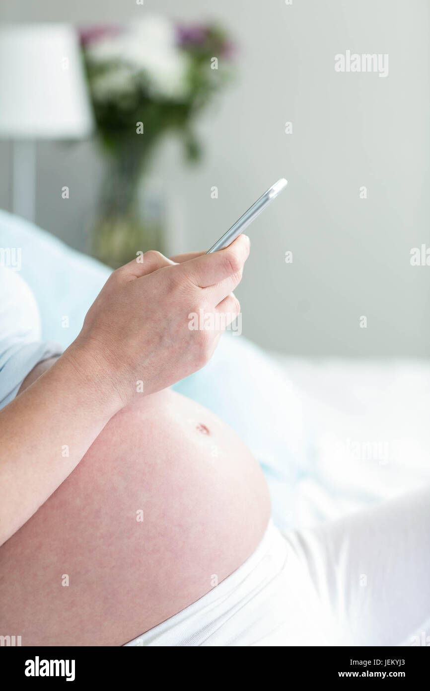 Pregnant woman lying in bed texting Stock Photo - Alamy