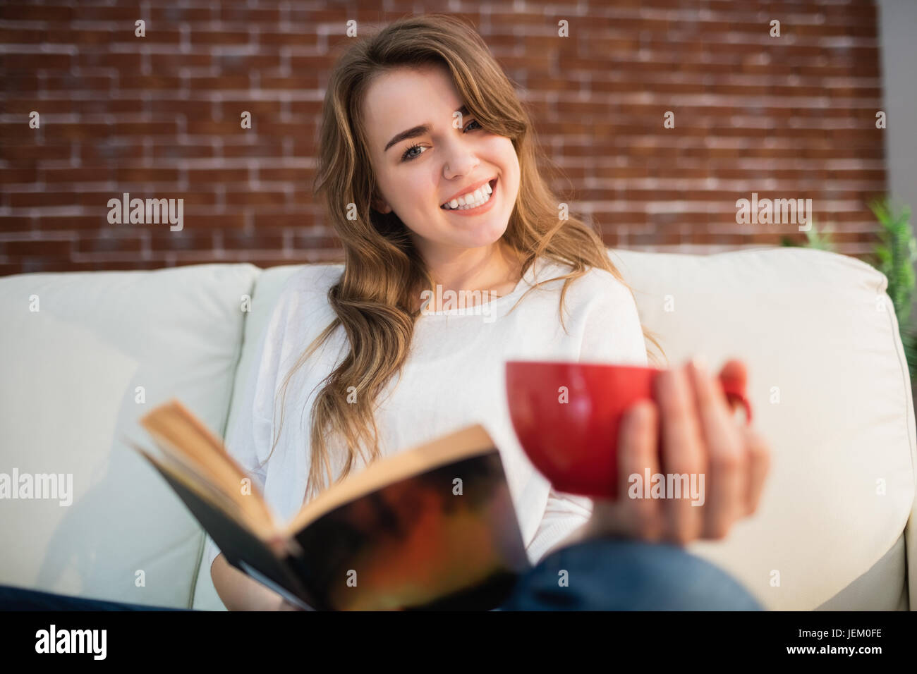Smiling woman reading a book while drinking Stock Photo - Alamy