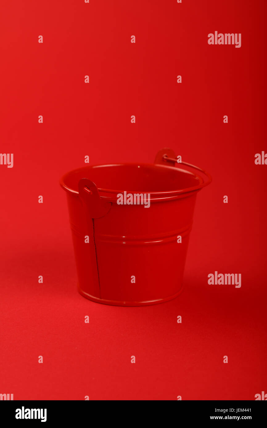 One small red painted metal empty toy bucket over red paper background ...