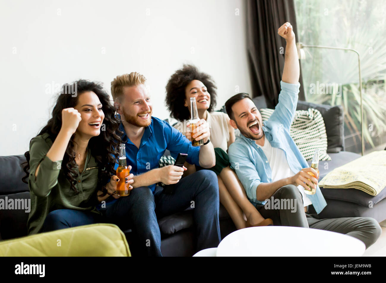 Group of friends watching TV , drinking cider and having fun in the ...
