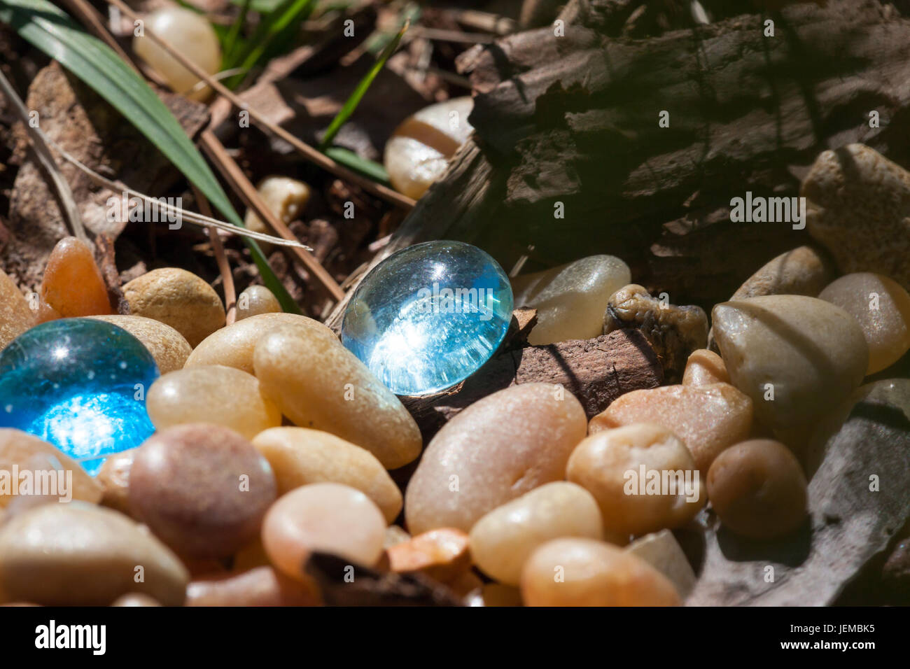Sunshine lights up two blue glass pebbles scattered among small tumbled ...