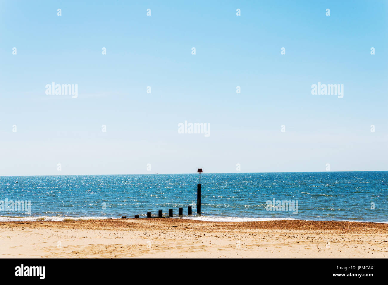 Dock pilings on a sandy beach, blue ocean and yellow sand, sunny hot ...