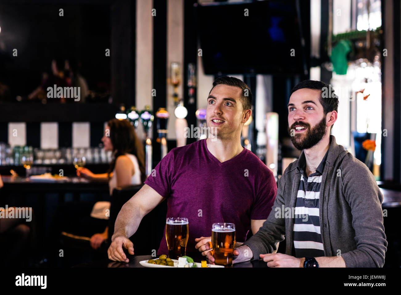 Friends having a pint and watching tv Stock Photo - Alamy
