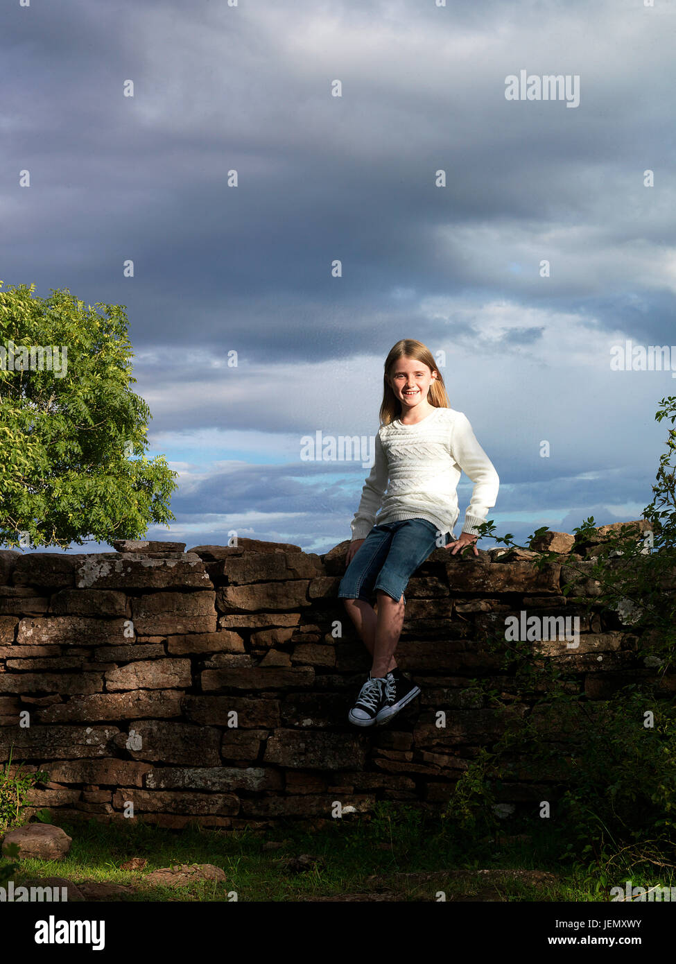 Girl sitting on stone wall Stock Photo - Alamy