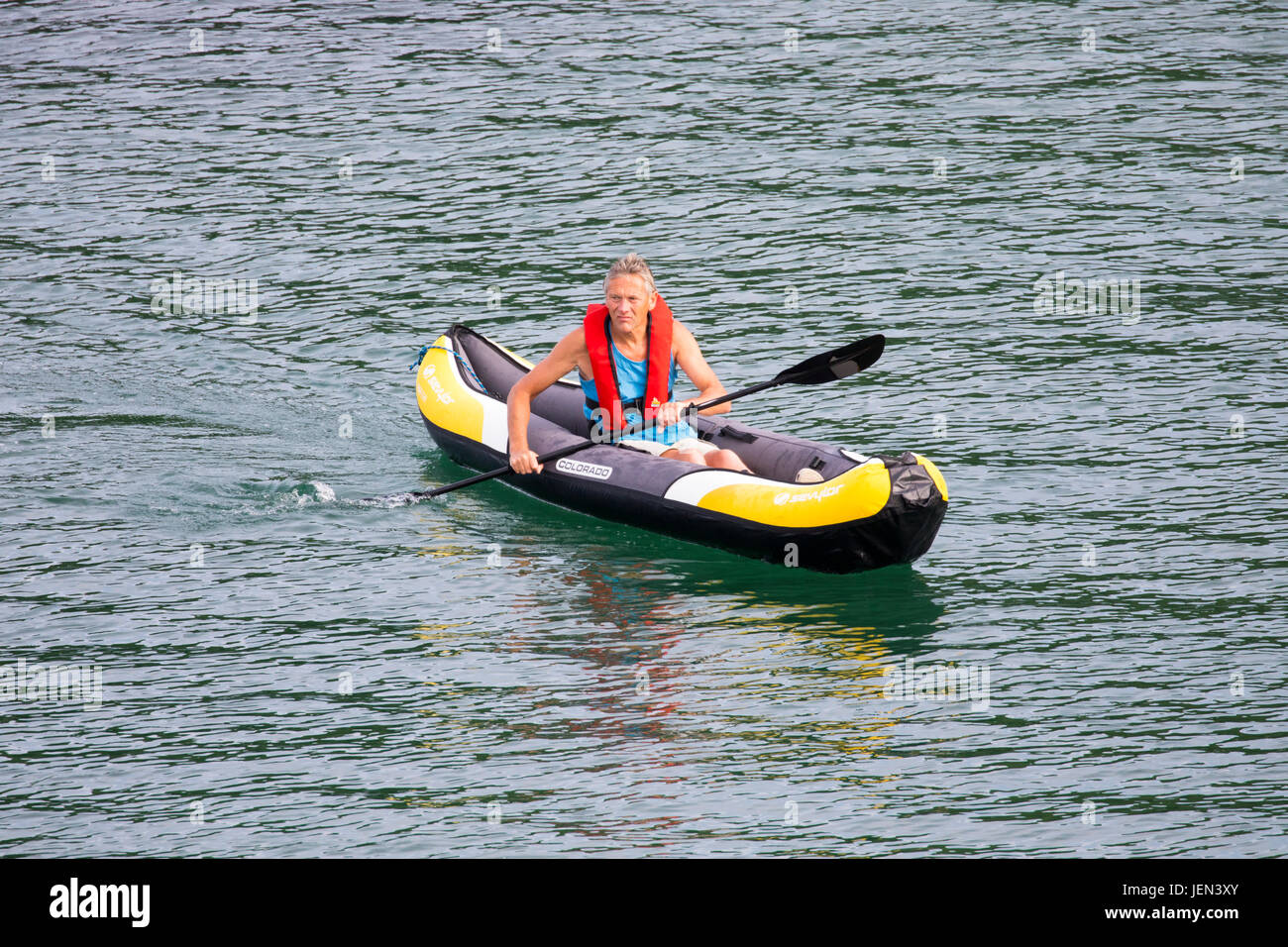 A person paddling in an inflatable canoe on the sea at the harbour of ...