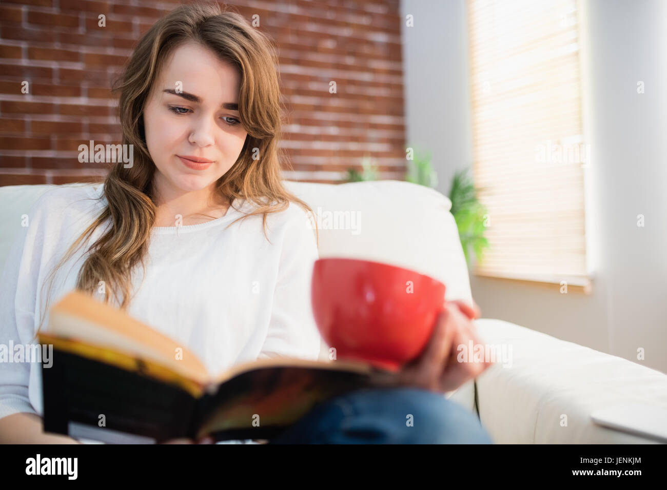 Focused woman reading a book while drinking Stock Photo - Alamy