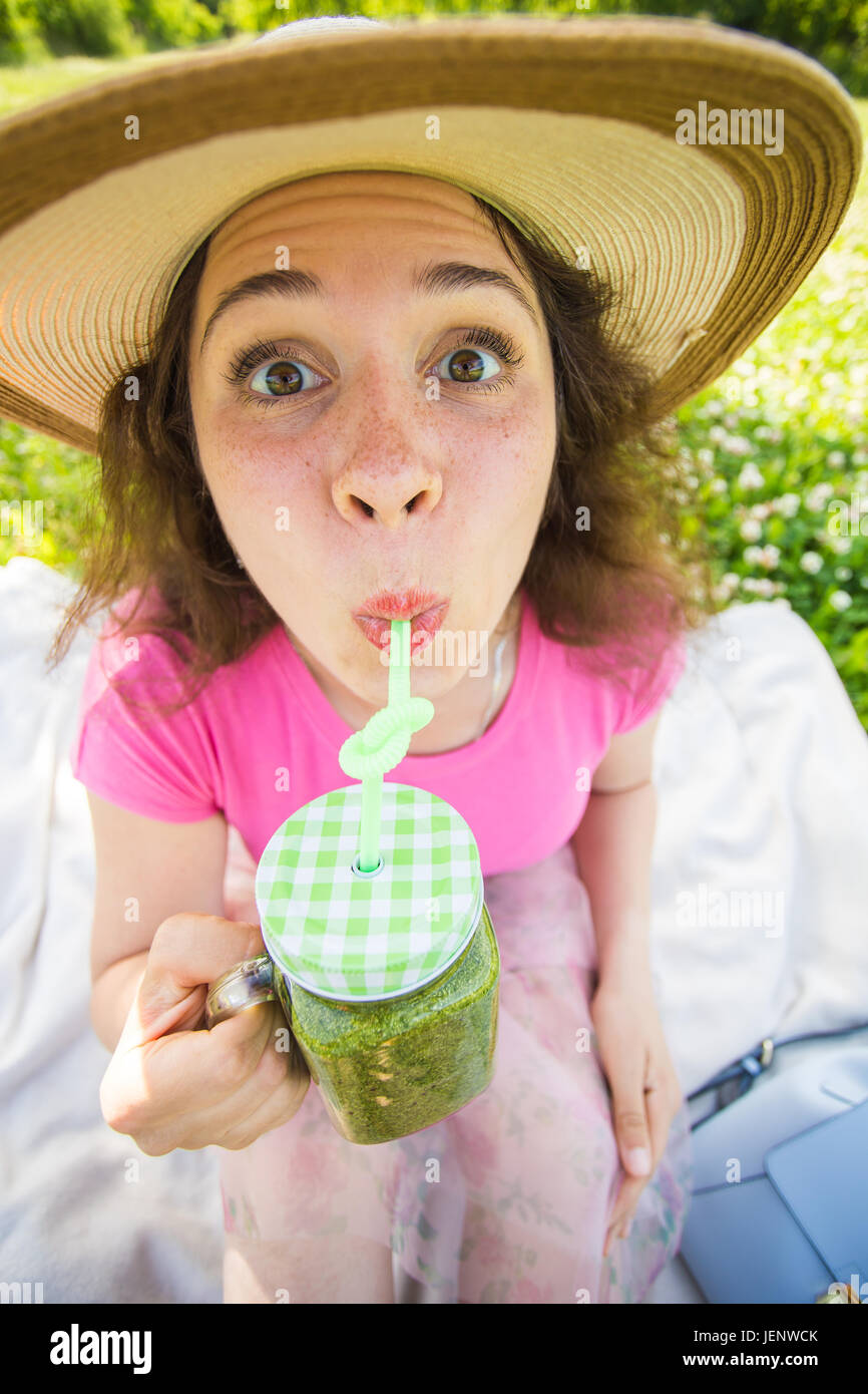Funny woman drinking green detox smoothie on picnic. Face close up ...