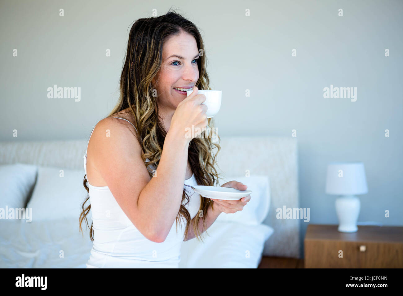 smiling woman sipping coffee on her bed Stock Photo - Alamy