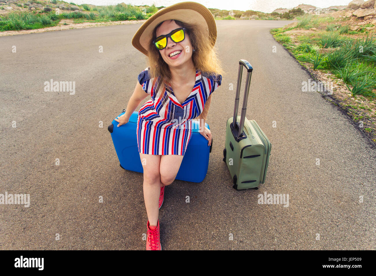 Happy Traveler Woman Sitting On A Suitcase On The Road And Smiling