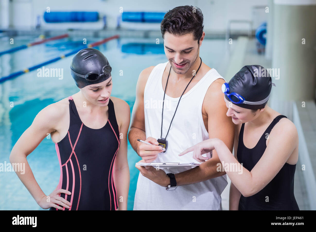 Smiling trainer showing clipboard at swimmers Stock Photo - Alamy