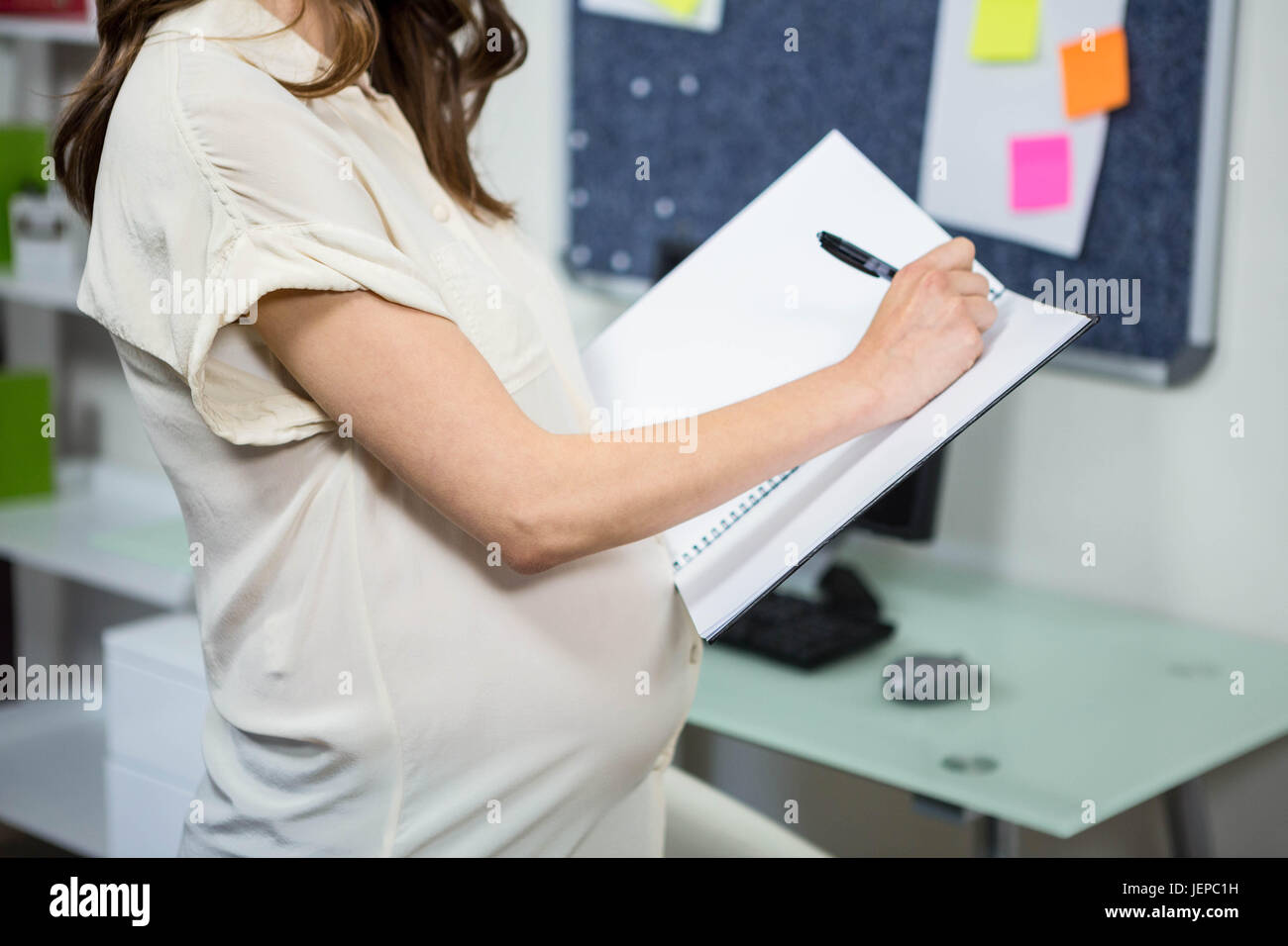 Pregnant businesswoman writing in folder Stock Photo - Alamy
