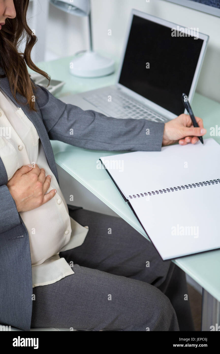 Pregnant businesswoman writing in folder Stock Photo - Alamy