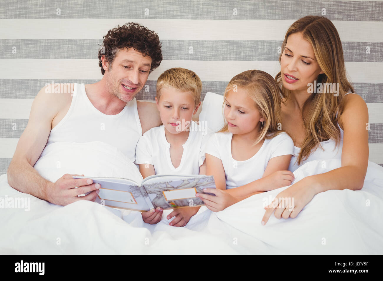 Family reading book on bed Stock Photo - Alamy