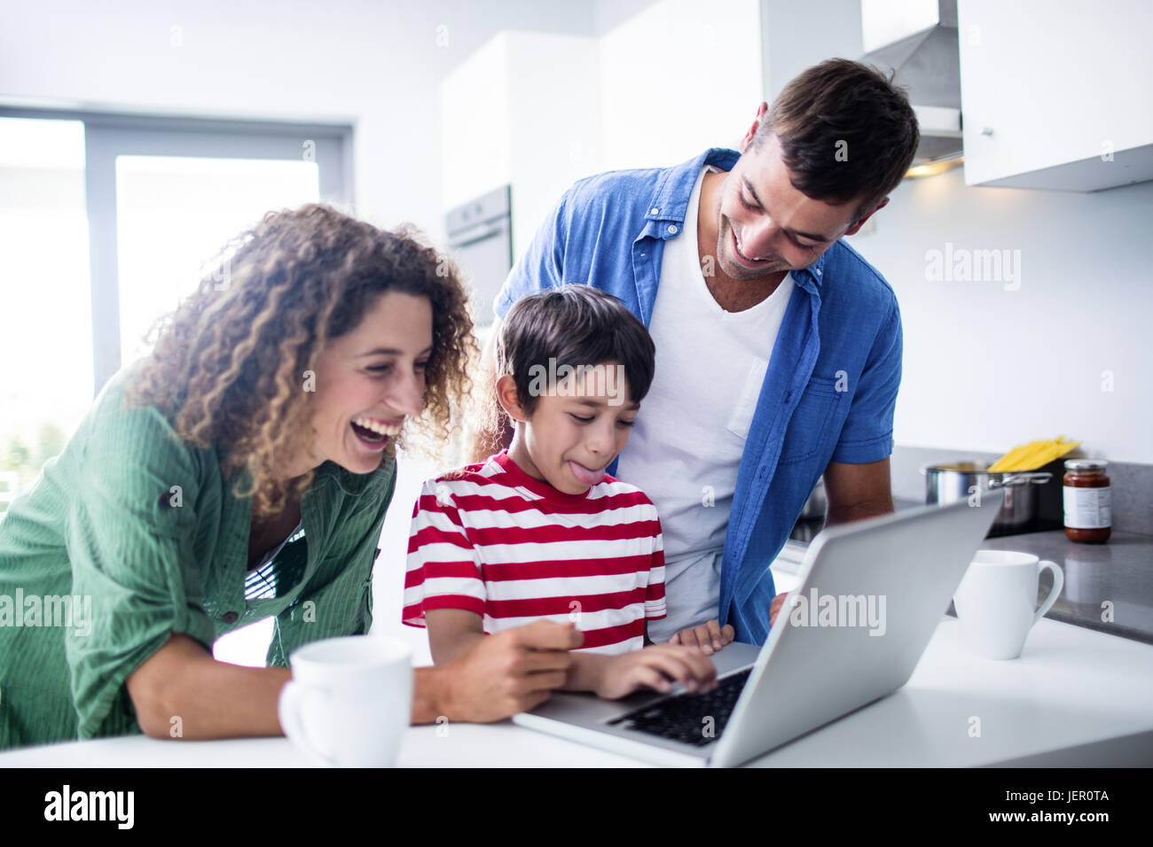 Parents using laptop with son in kitchen Stock Photo - Alamy