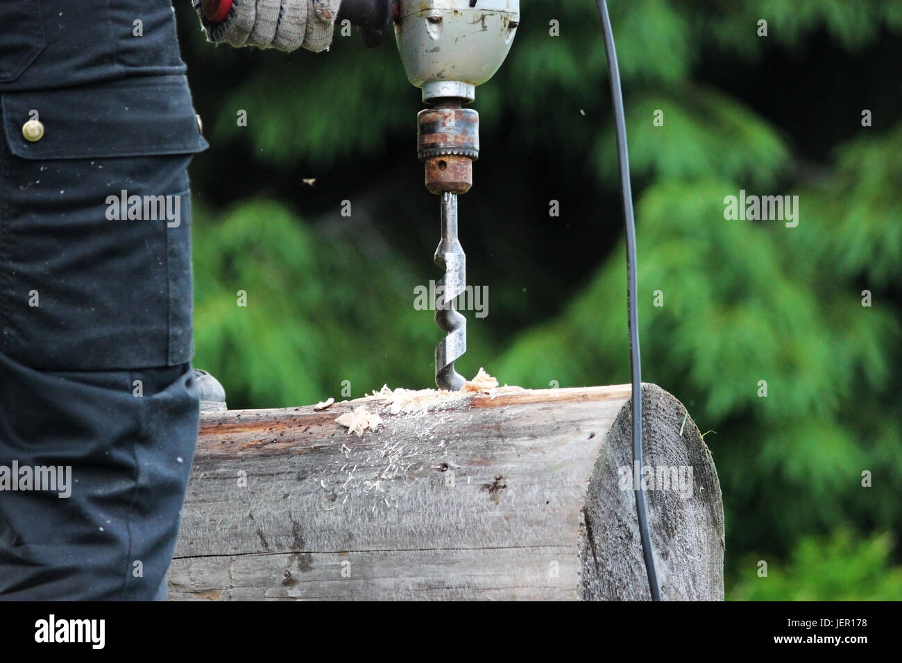 The worker collects the frame and drills a hole in a log for dowel ...