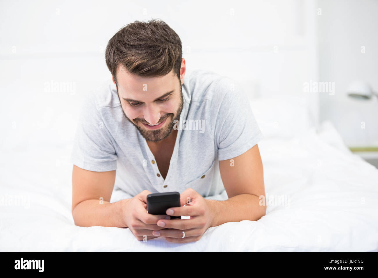 Happy man using mobile phone on bed Stock Photo - Alamy