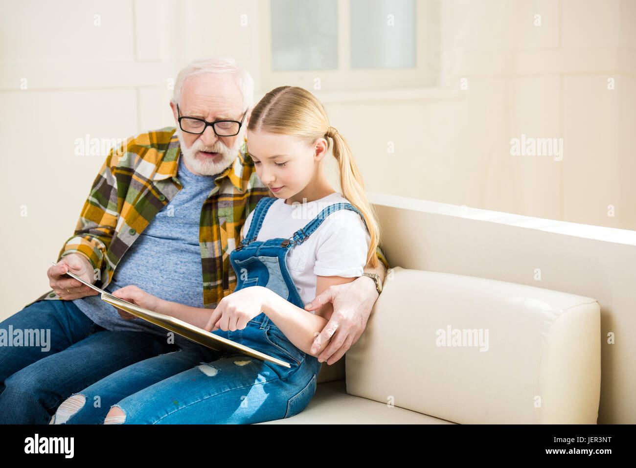 Happy grandfather and granddaughter reading book together at home Stock ...