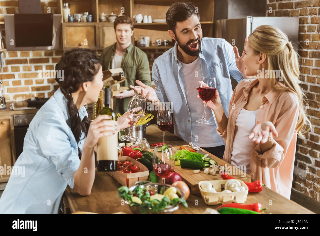 young people partying at kitchen, drinking wine, having food at home ...