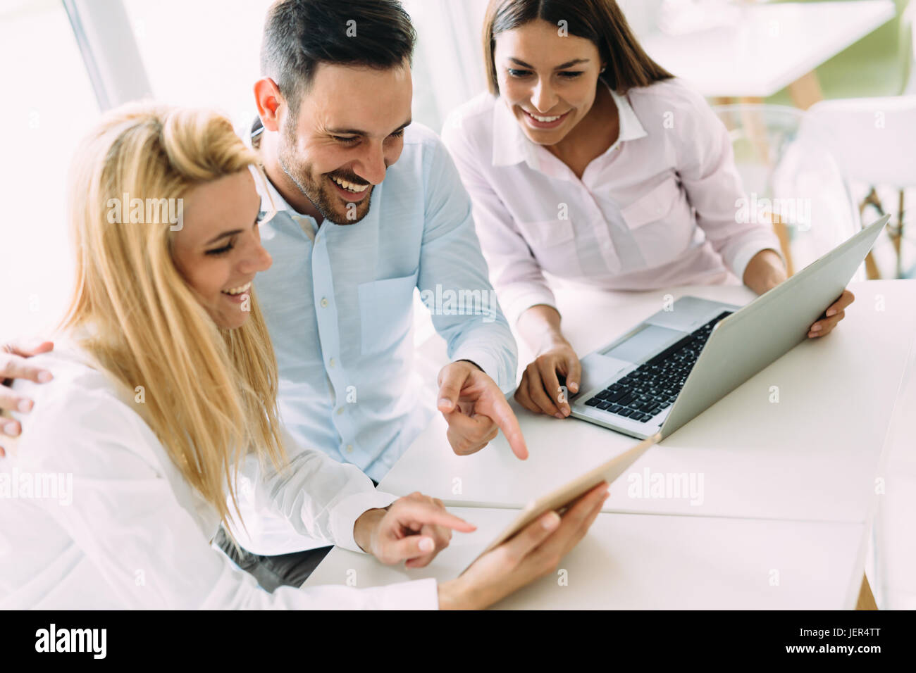Three young smiling cheerful colleagues working together on laptop ...